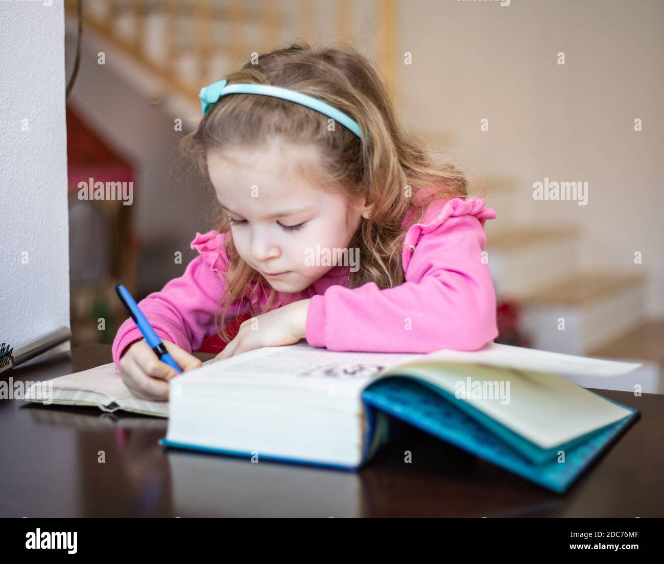 Little blonde girl reading and doing homework Stock Photo - Alamy