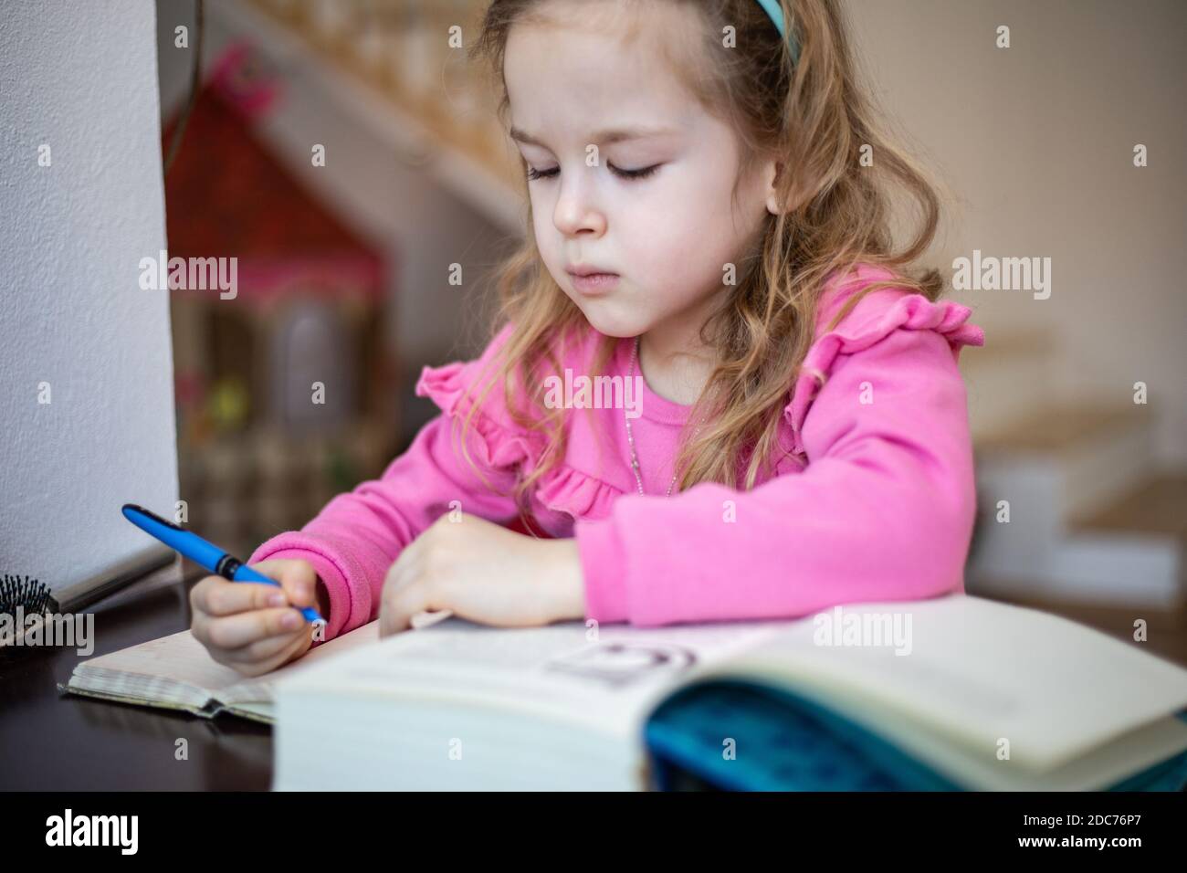Little blonde girl reading and doing homework Stock Photo - Alamy
