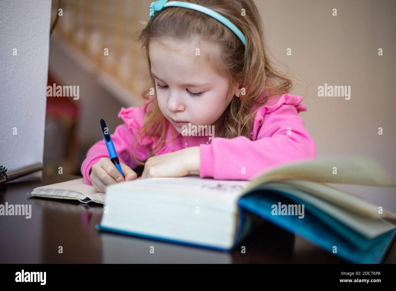 Little blonde girl reading and doing homework Stock Photo - Alamy