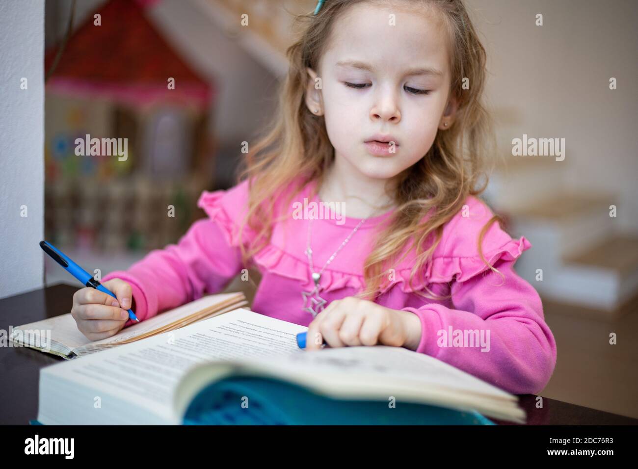 Little blonde girl reading and doing homework Stock Photo - Alamy