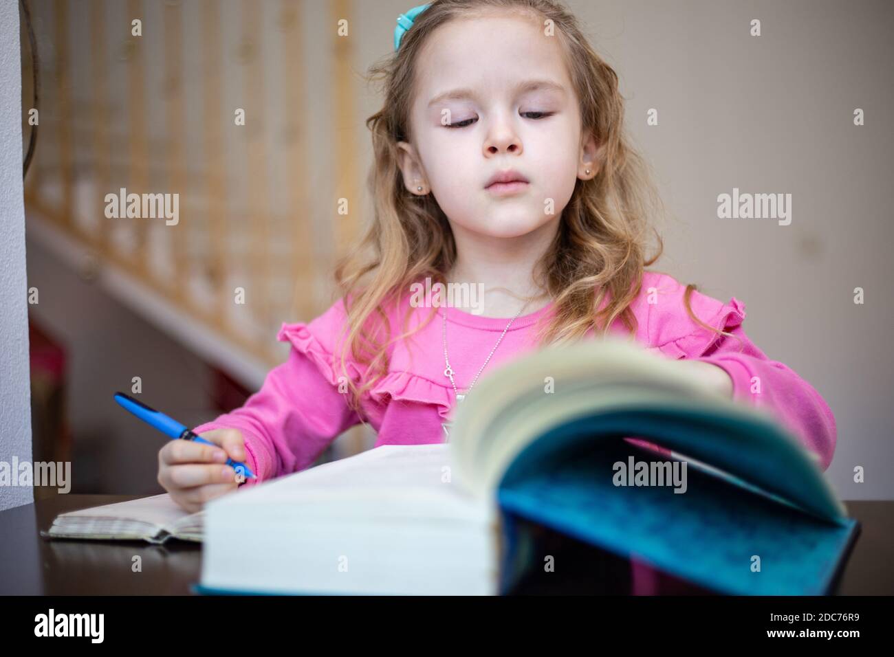 Little blonde girl reading and doing homework Stock Photo - Alamy