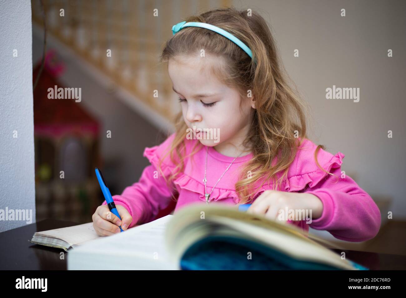 Little blonde girl reading and doing homework Stock Photo - Alamy