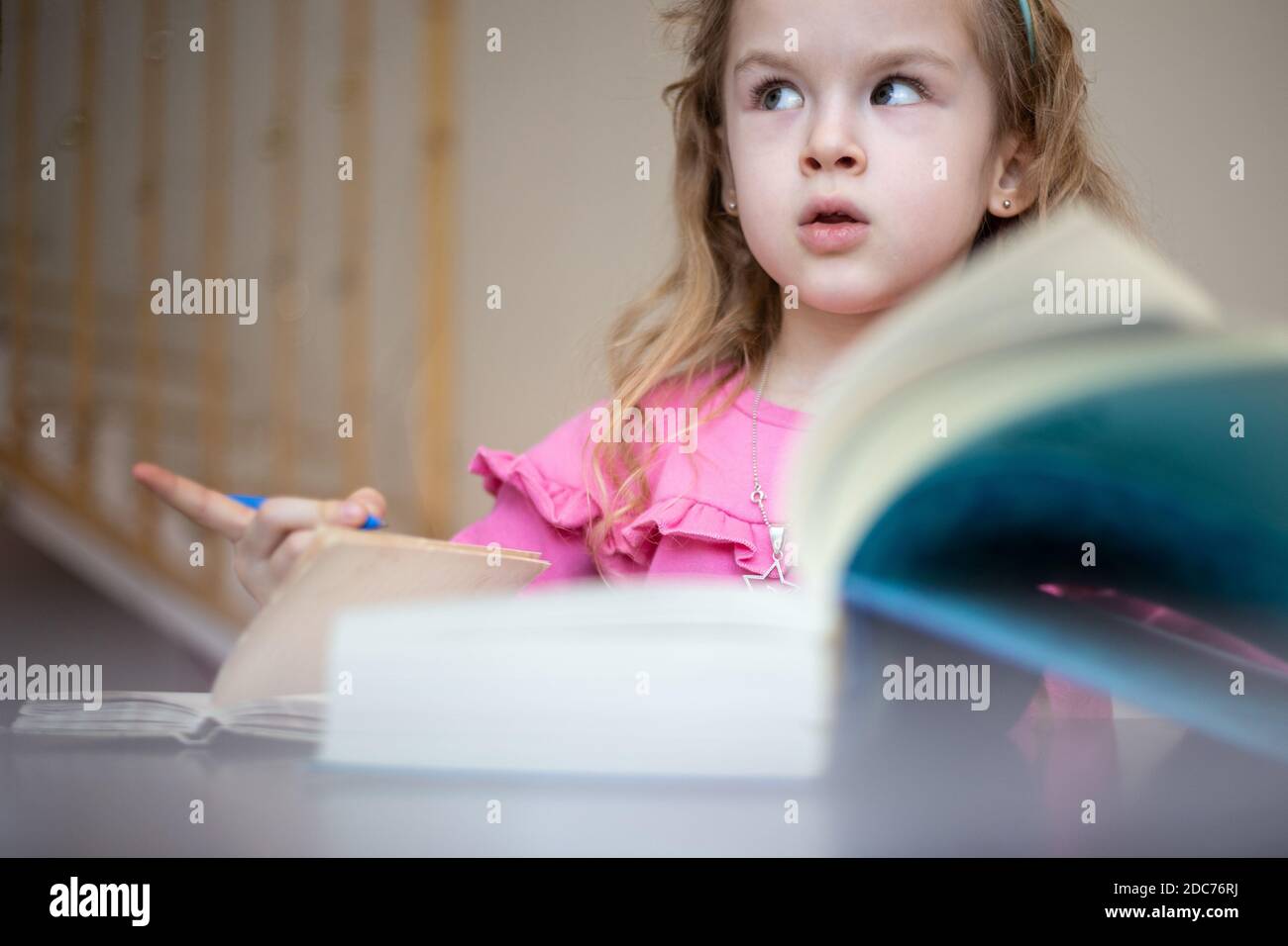 Little blonde girl reading and doing homework Stock Photo - Alamy