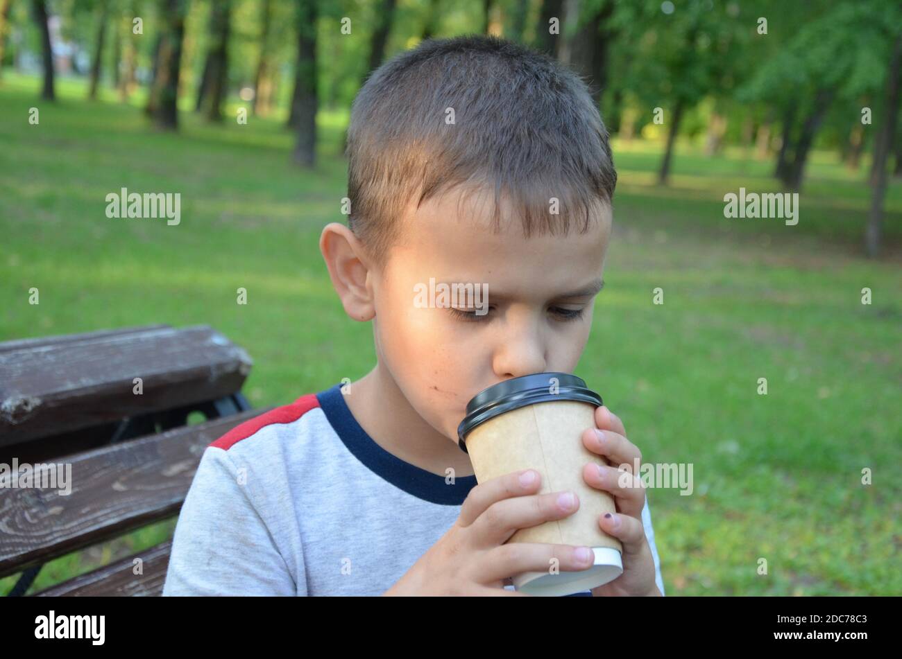 boy in the park on a bench drinking coffee in a paper cup. the kid ...