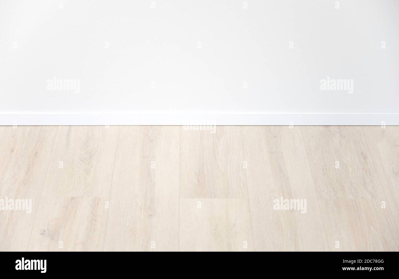 light oak laminate with white baseboard and white wall as background ...