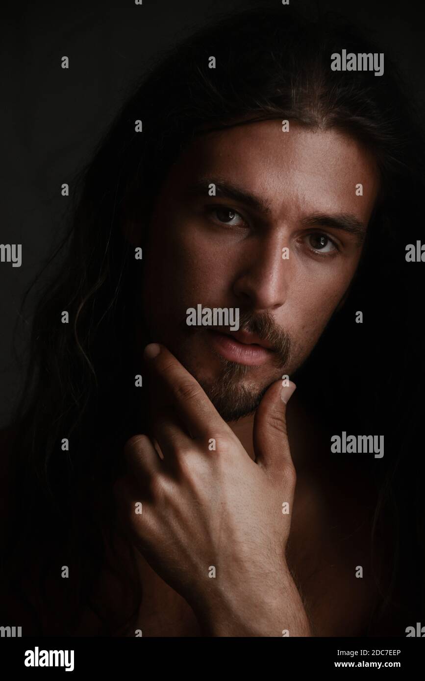 Handsome young man with long hair with hand on chin Stock Photo - Alamy