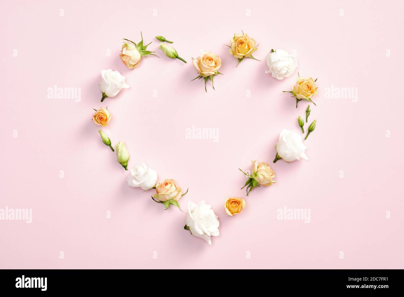 Heart symbol made of roses flowers and leaves on pastel pink background ...