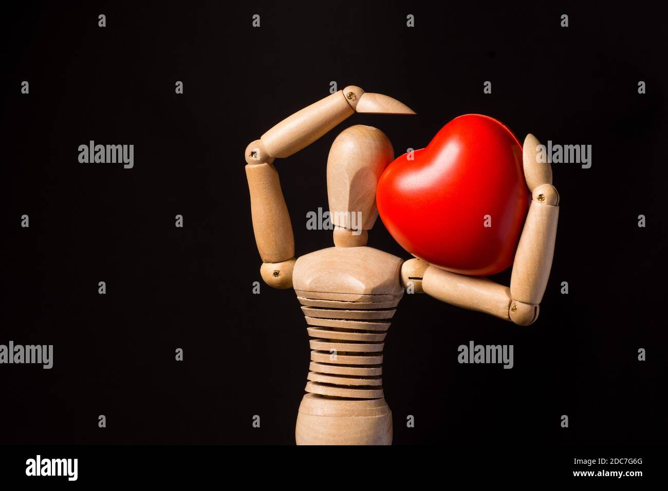 Wooden puppet with a big red heart in his hands on a black background ...