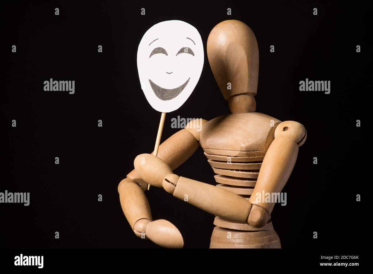 Wooden puppet doll on hinges holds a mask in hands and covers her face ...