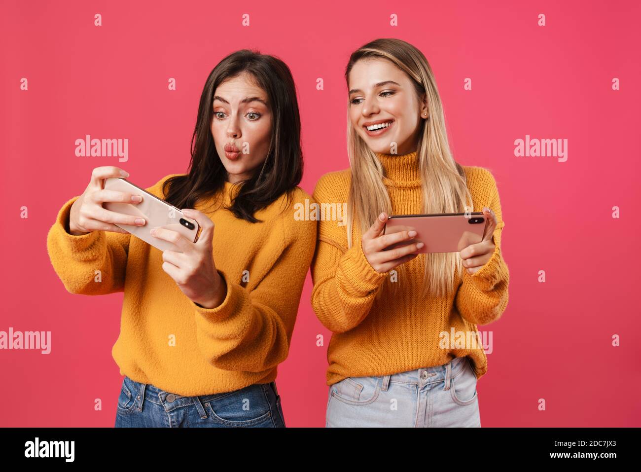 Two happy pretty girls using mobile phones isolated over pink ...