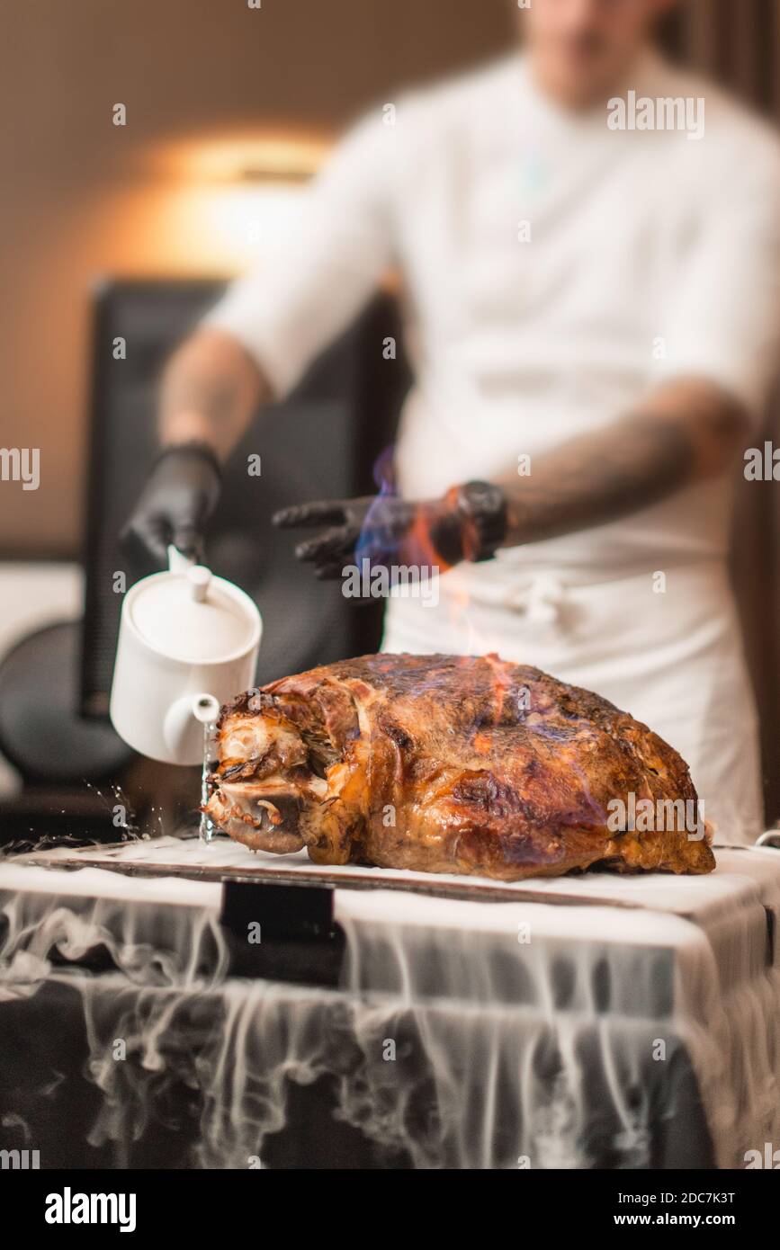 Chef, pouring alcohol into a frying table with meat. Cold ice smoke ...