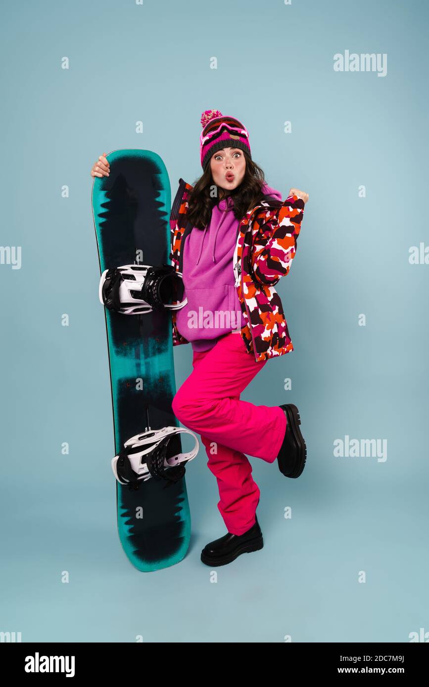 Surprised sportswoman making kiss lips while posing with snowboard ...