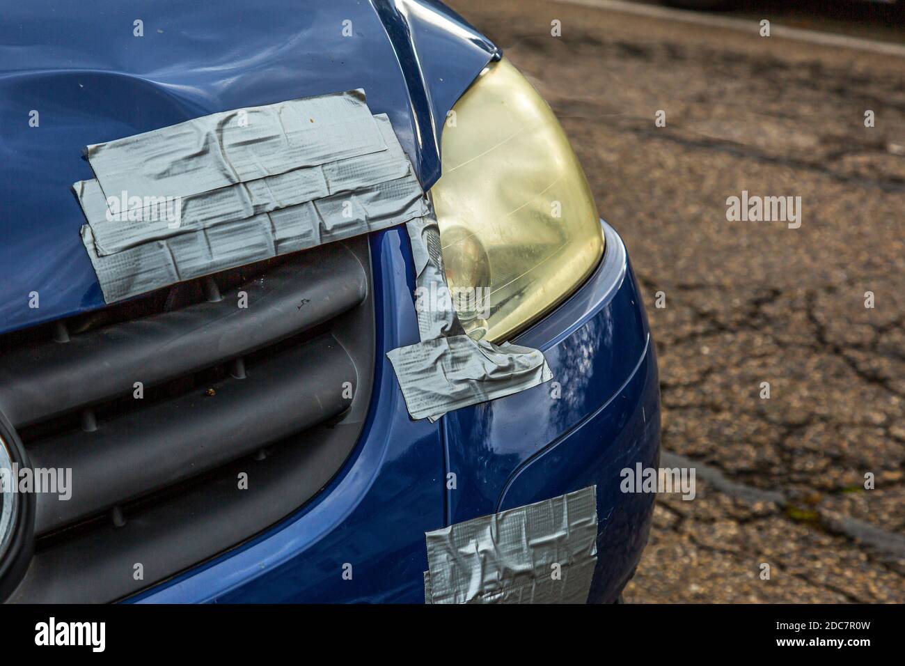A deformed bonnet of a blue car is provisionally repaired with an ...