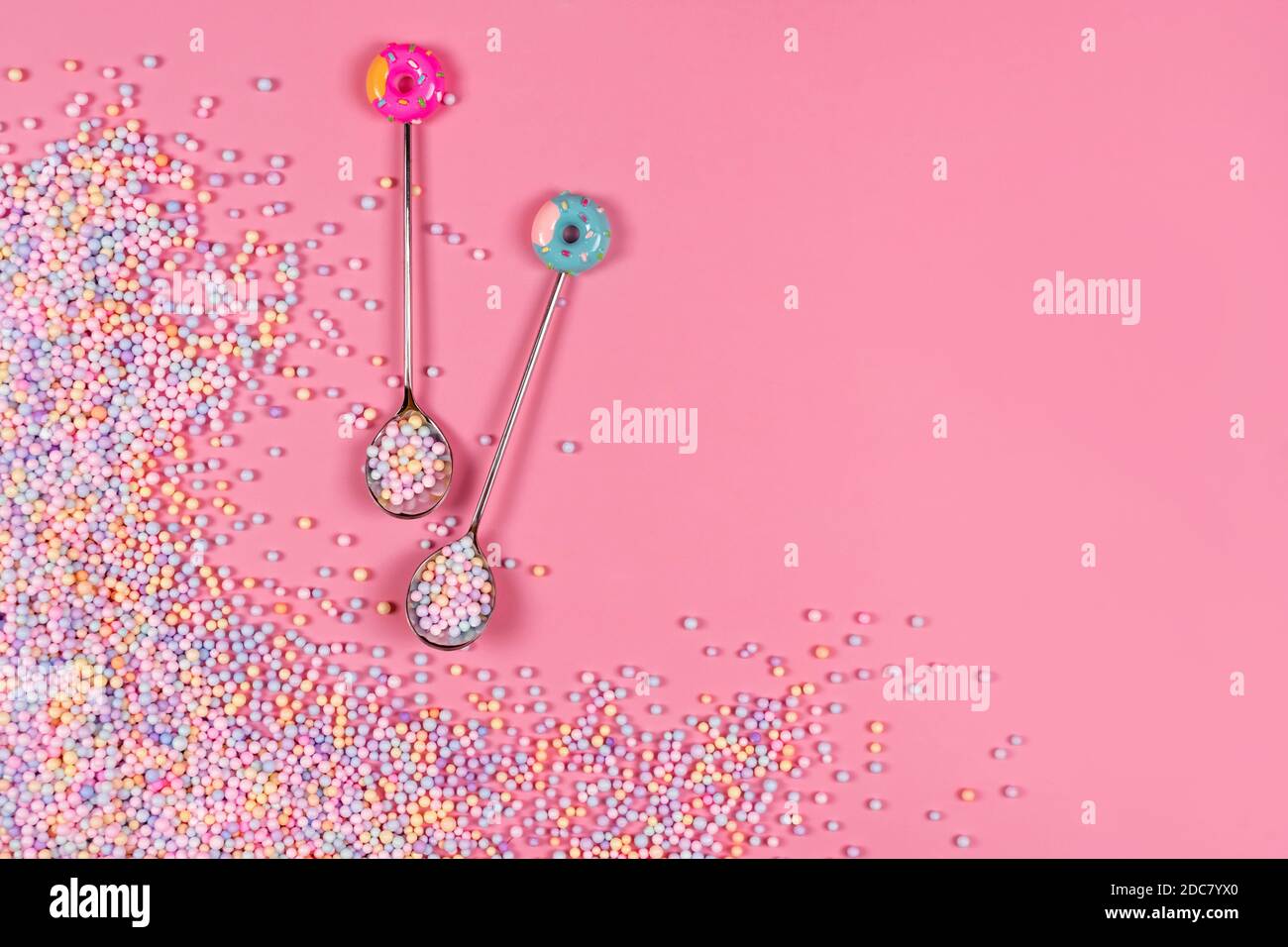 Pile of pastel color sugar balls with spoons on pink background with ...