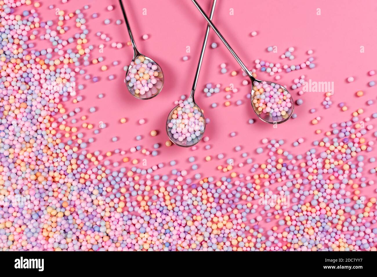 Pile of pastel color sugar balls with spoons on pink background. Mixed ...