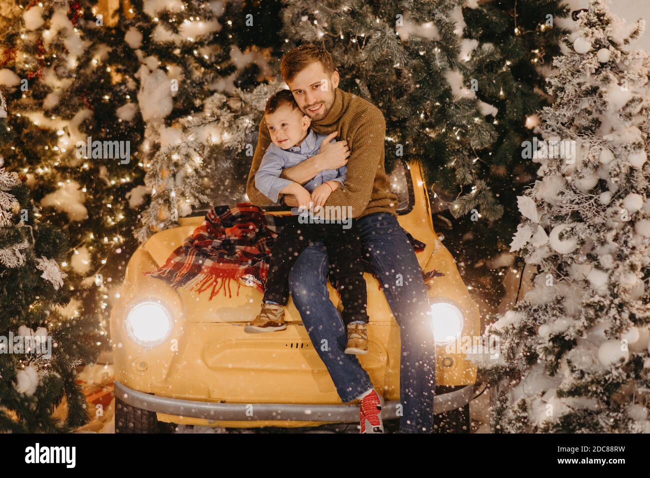 Father and son sit on a retro car hood and have a fun near Christmas ...