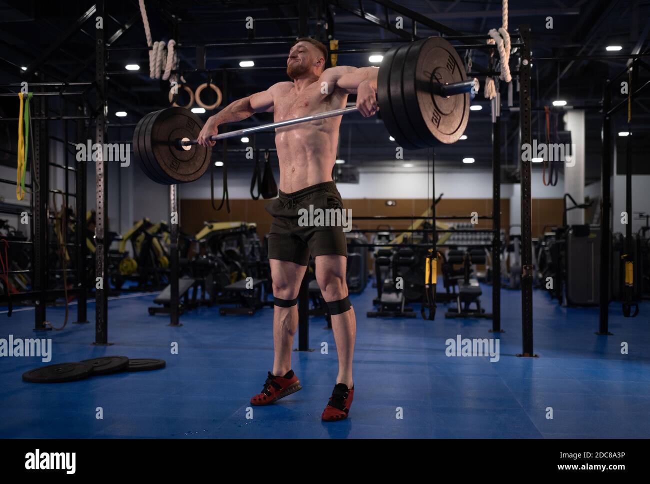 Aggressive male athlete deadlifting heavy barbell with effort in dark ...