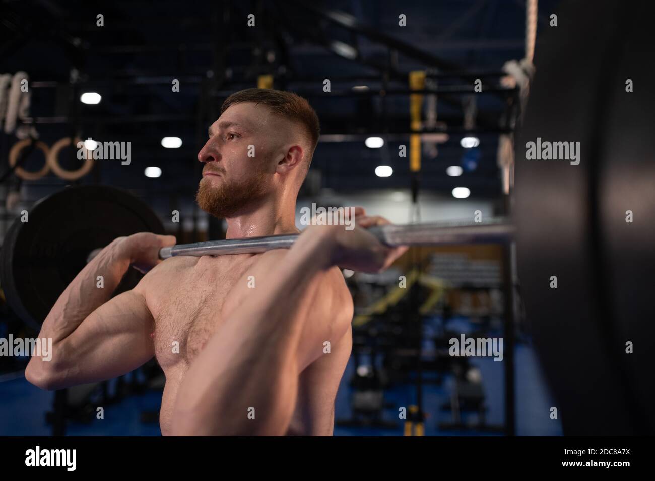 Strained shirtless man exercising with barbell during weightlifting ...