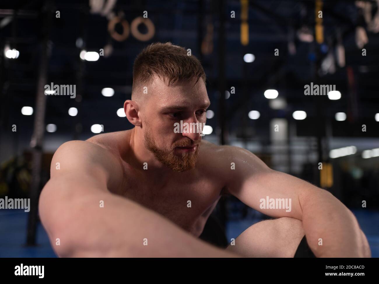 Tired weightlifter sitting and relaxing after intense training in dark ...