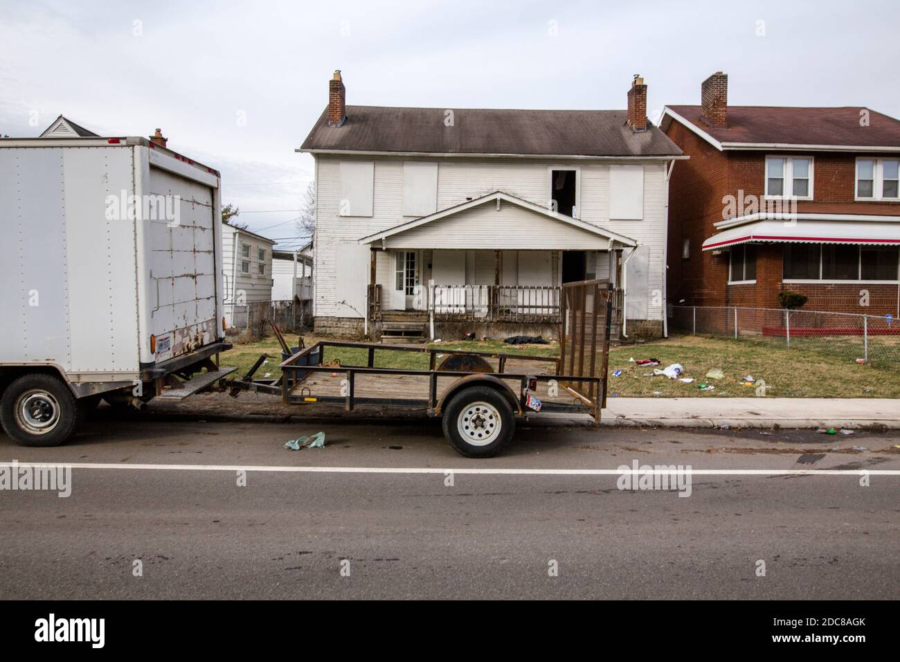 A flatbed trailer sits in front of abandoned home in trash-filled yard ...