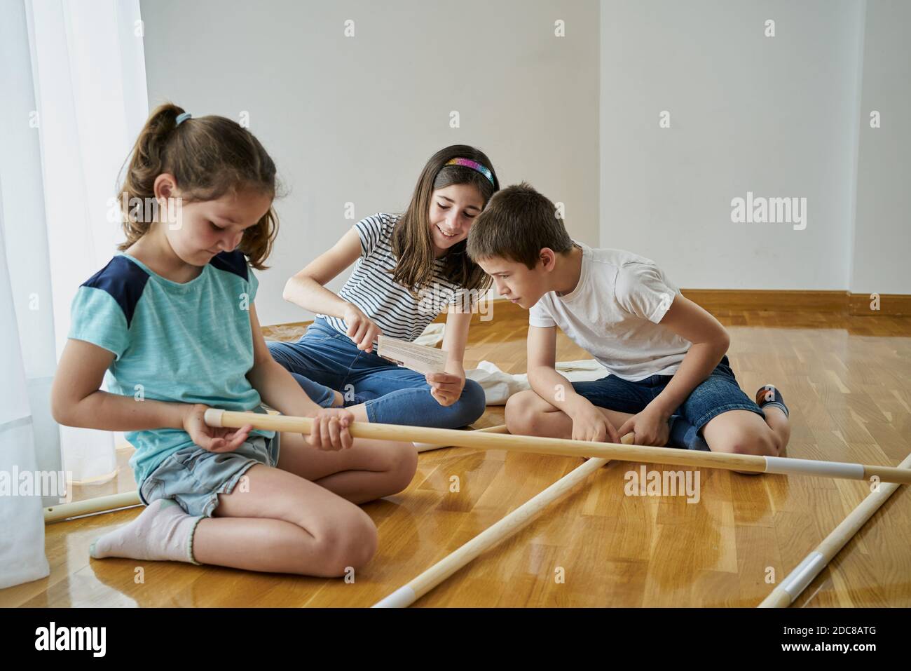 Children putting the sticks to build a teepee tent inside their house ...