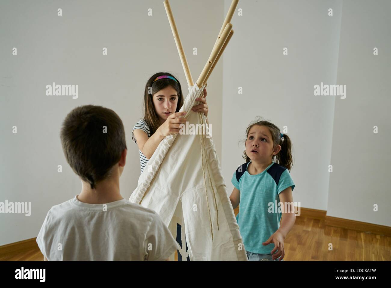 Children putting the sticks to build a teepee tent inside their house ...