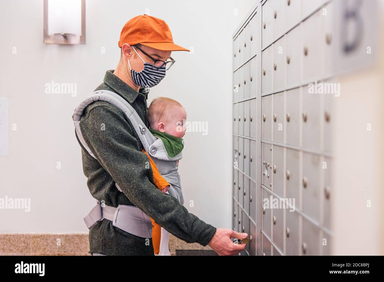 Father wearing face mask opening locker in room while carrying baby ...