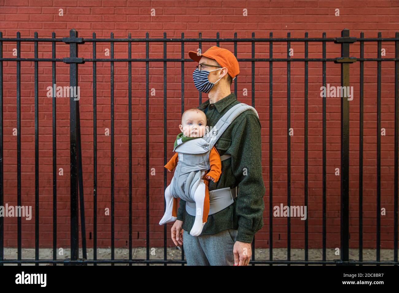 Father wearing face mask carrying cute daughter in baby carrier while ...