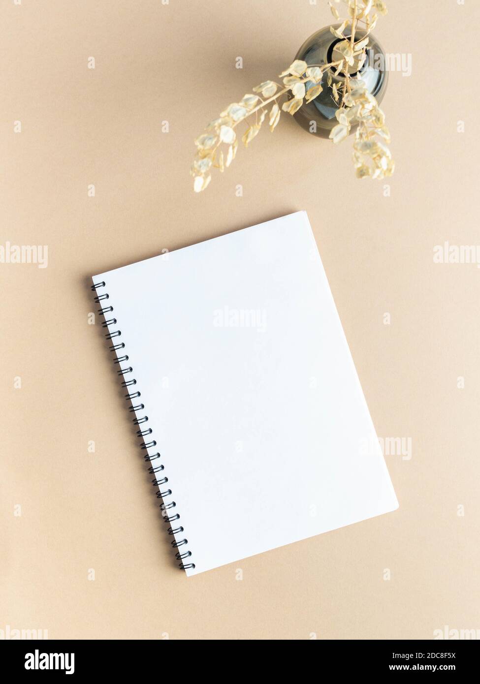 White blank notepad sheet with spiral and glass vase with dry plants on ...
