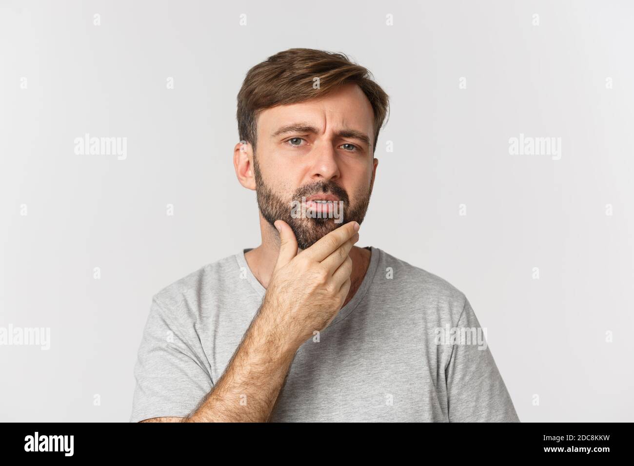 Close-up of confused man touching his beard and looking at himself ...