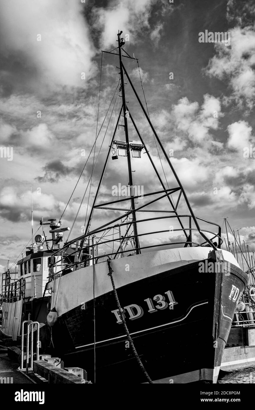 A trawler is moored alongside a wharf with its mast pointing upwards. A ...