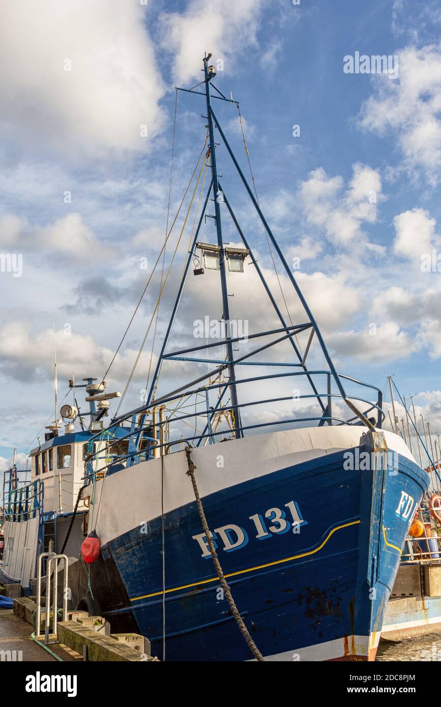 A trawler is moored alongside a wharf with its mast pointing upwards. A ...