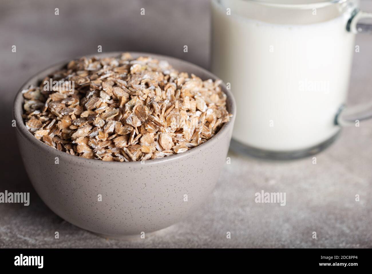 Rye flakes in a bowl with glass of milk on a stone background. Healthy ...