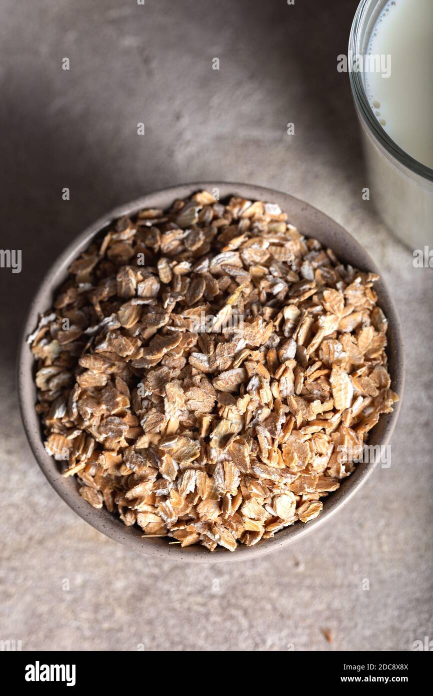 Rye flakes in a bowl with glass of milk on a stone background. Healthy ...