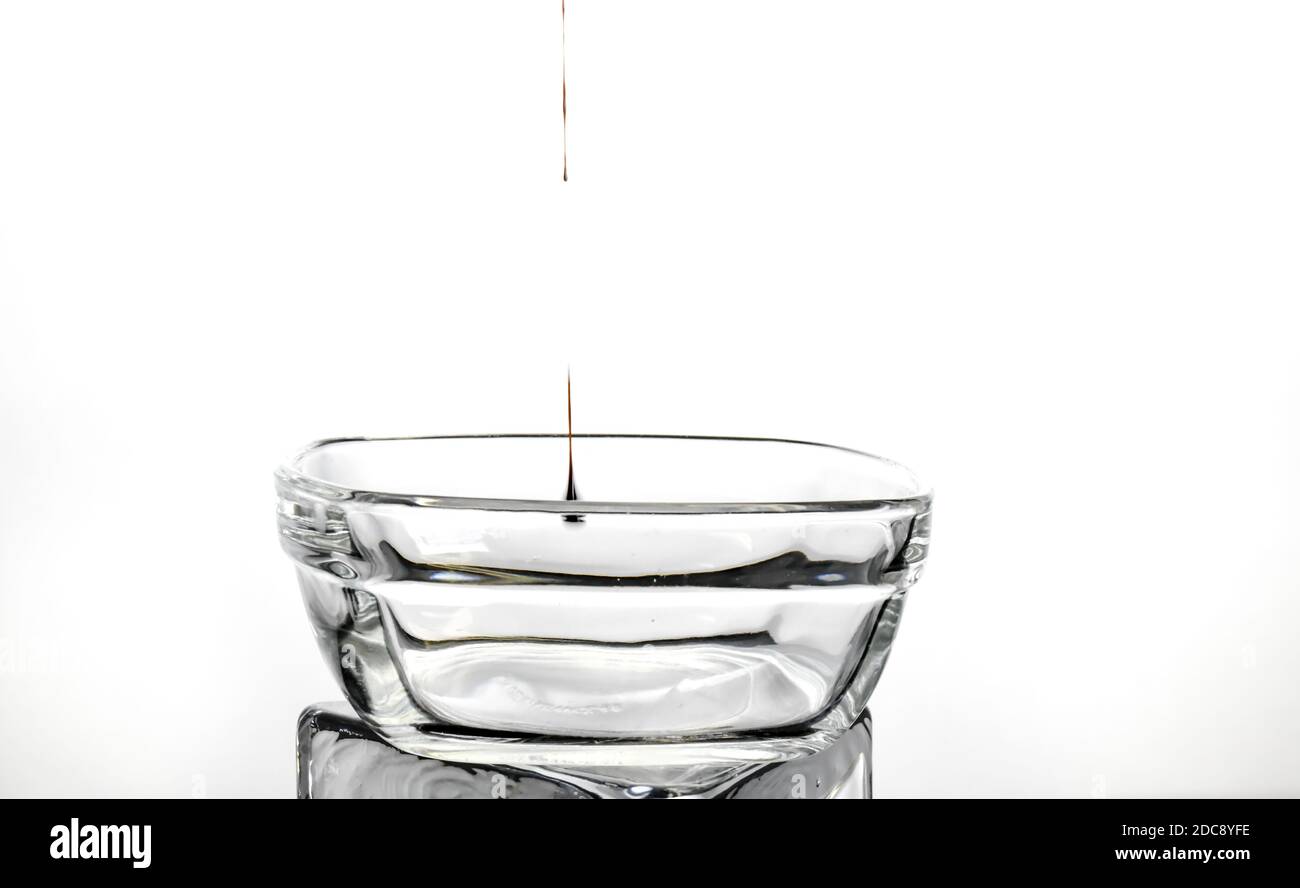 close-up of drop of olive oil falling into clear dish against white ...
