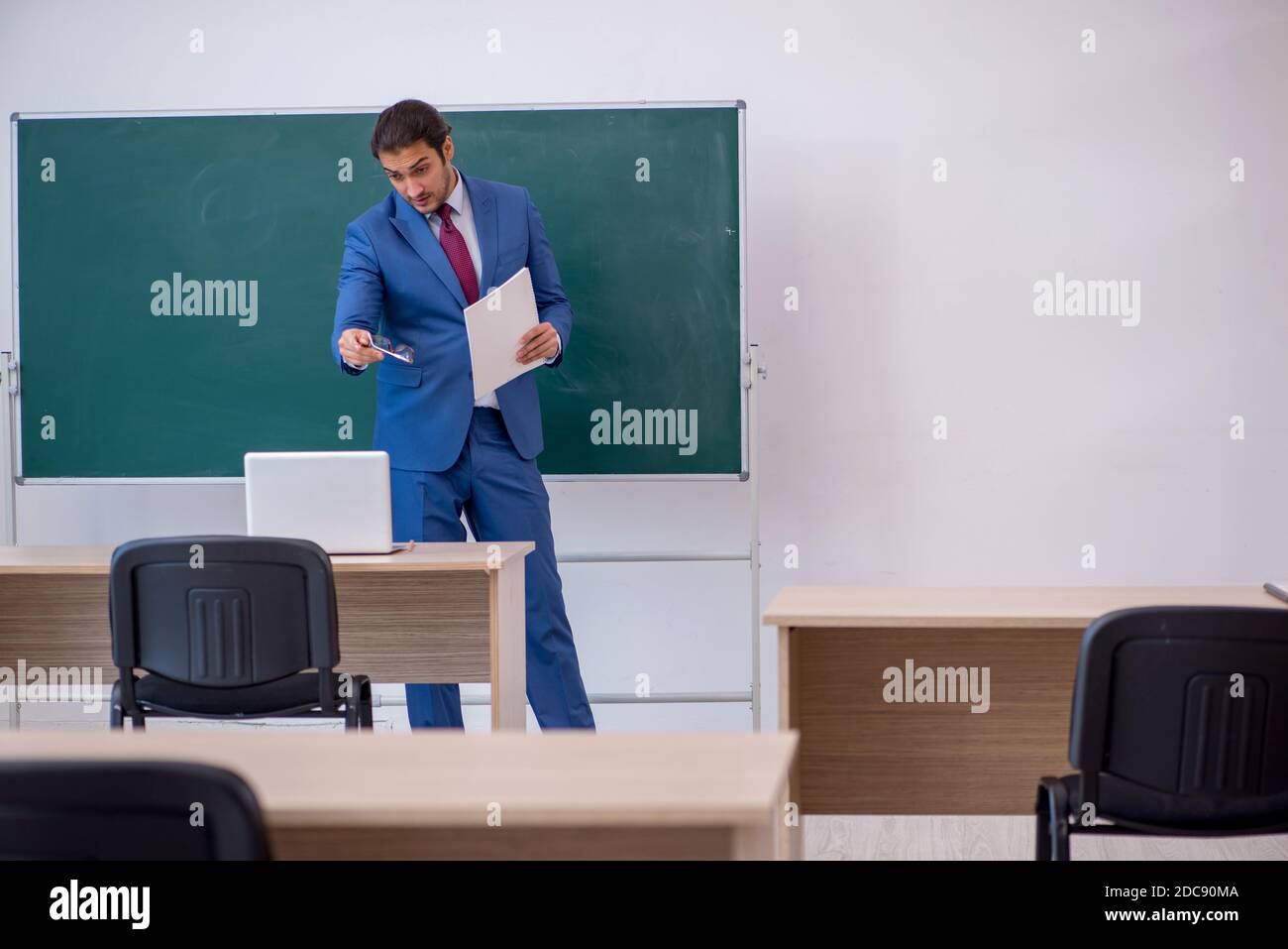 Young teacher in suit in front of green board Stock Photo - Alamy