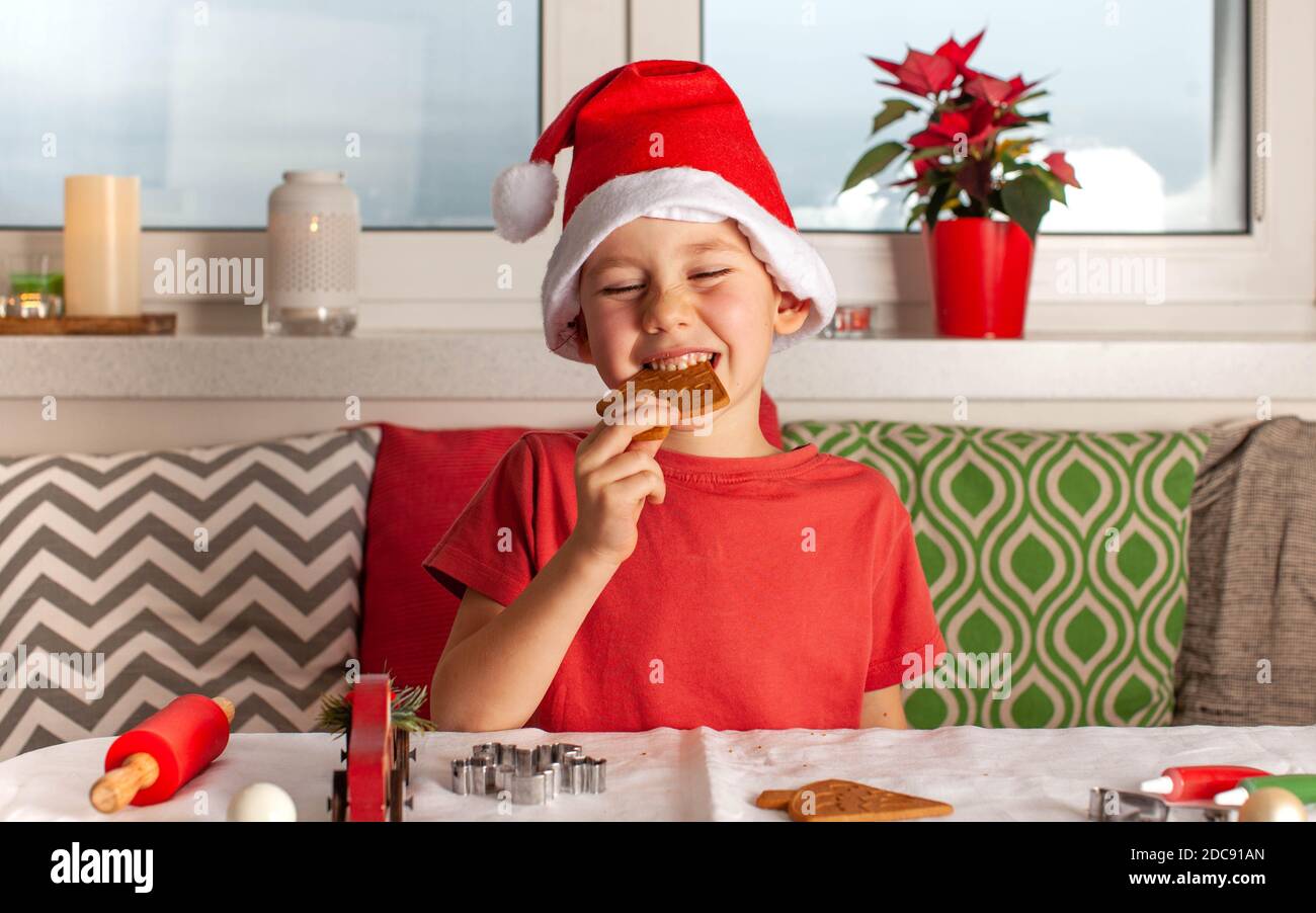 Happy boy in Santa Claus hat eating Christmas gingerbread. Cooking new ...