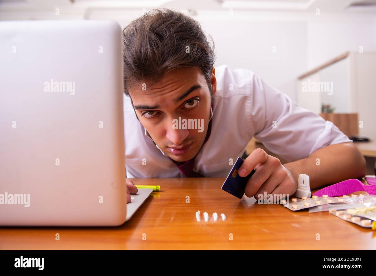 Young drug addicted male employee sitting at workplace Stock Photo - Alamy
