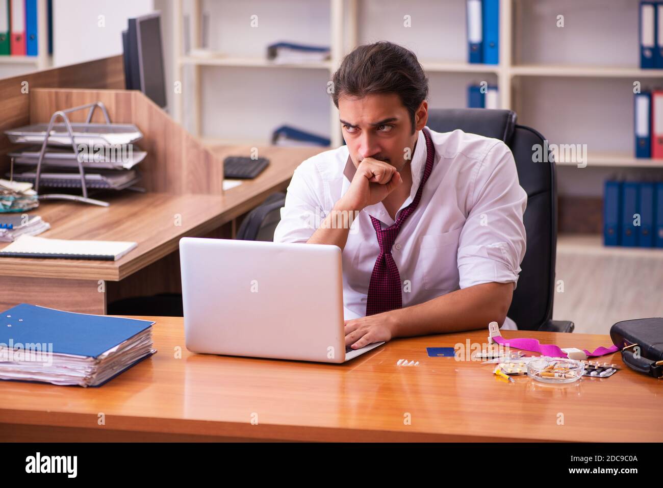 Young drug addicted male employee sitting at workplace Stock Photo - Alamy
