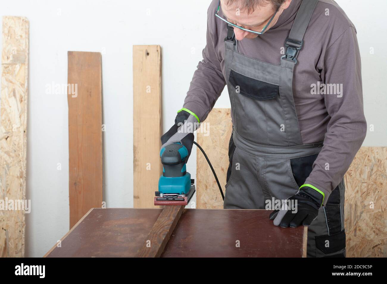 Carpenter working with electric sheet finishing sander on wood lath on ...