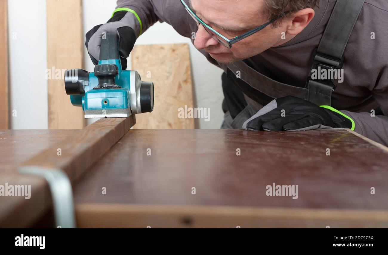 Carpenter working with electric planer on wood lath on desk, on ...
