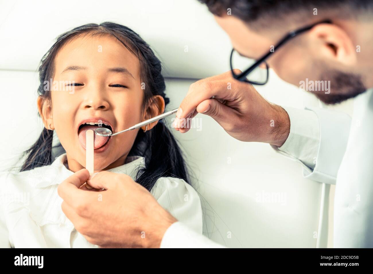 Friendly young dentist examining happy child teeth in dental clinic ...