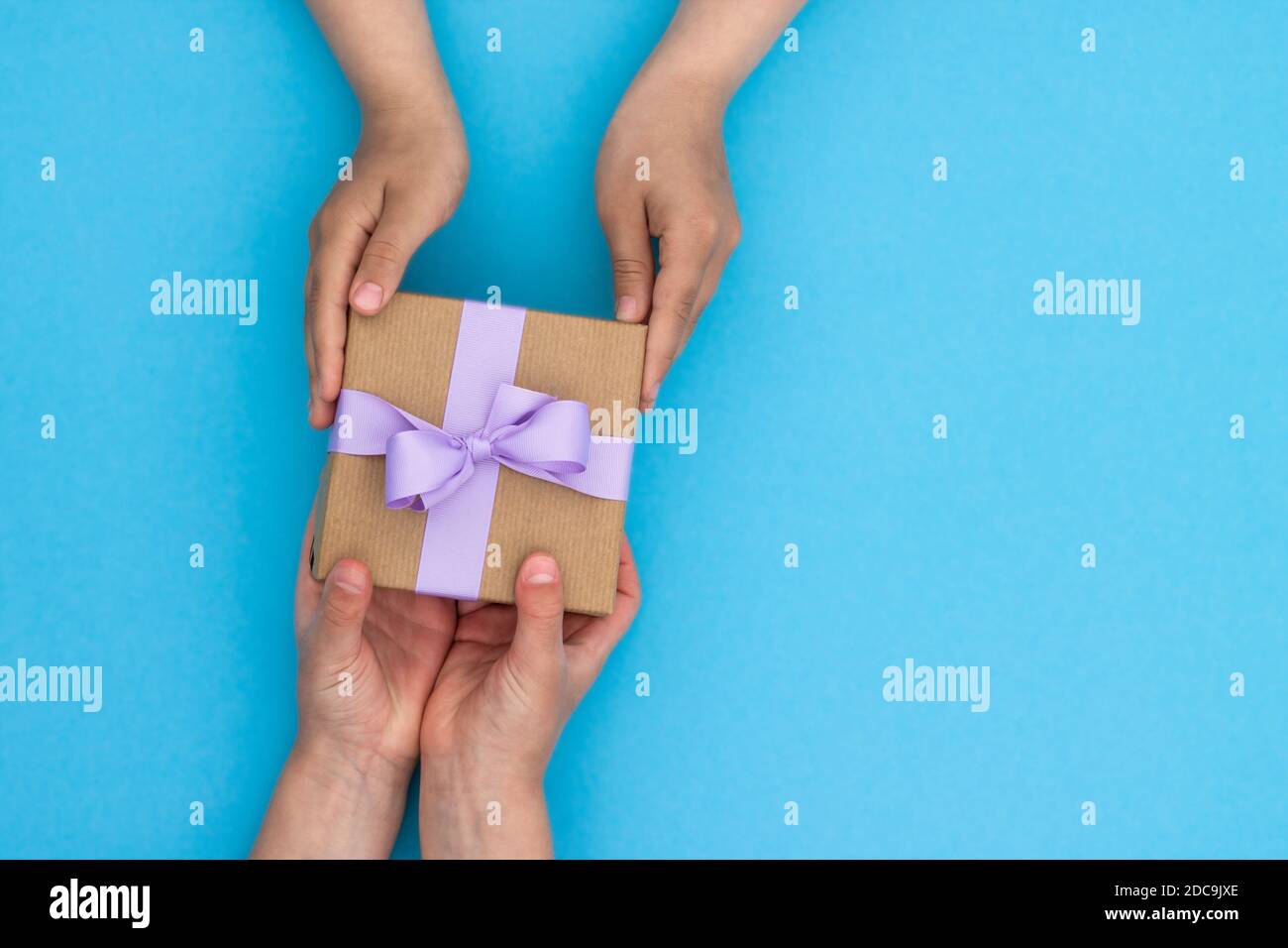 Hands giving or receiving a gift in craft paper with a lilac ribbon on ...