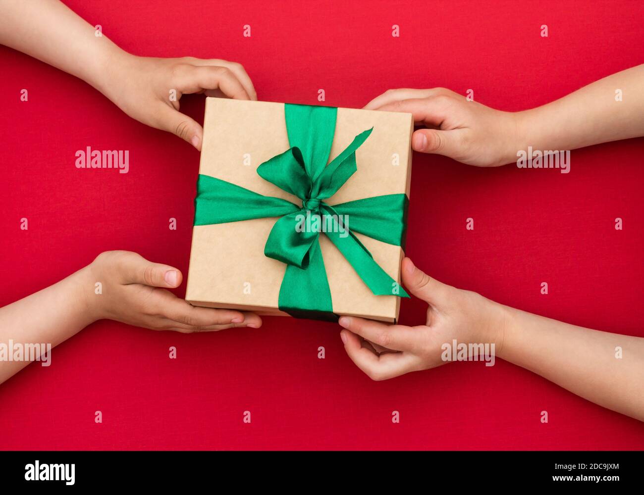 Hands giving or receiving a gift in craft paper with a green ribbon on ...