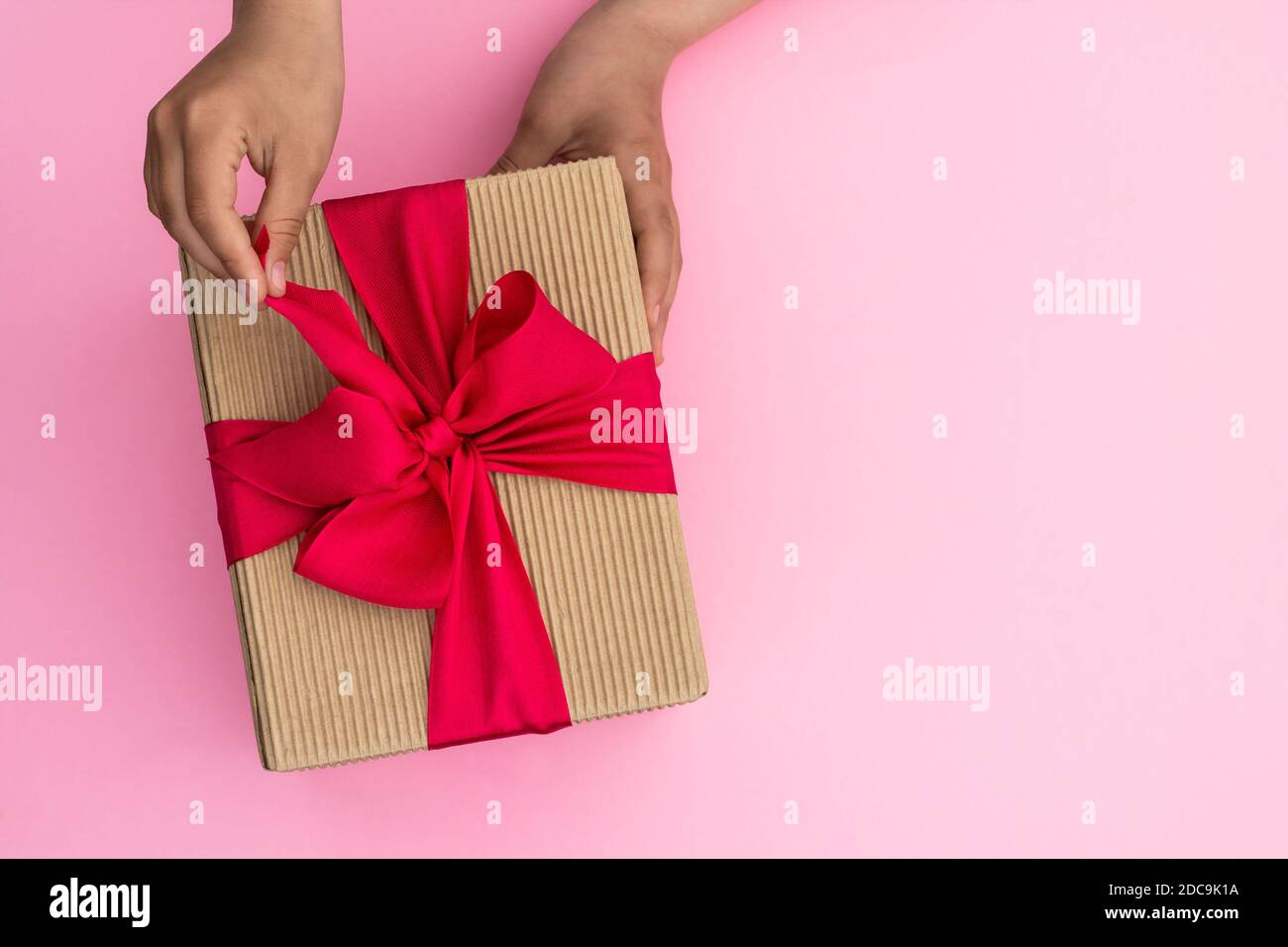 Hands giving or receiving a gift in craft paper with a pink ribbon on ...