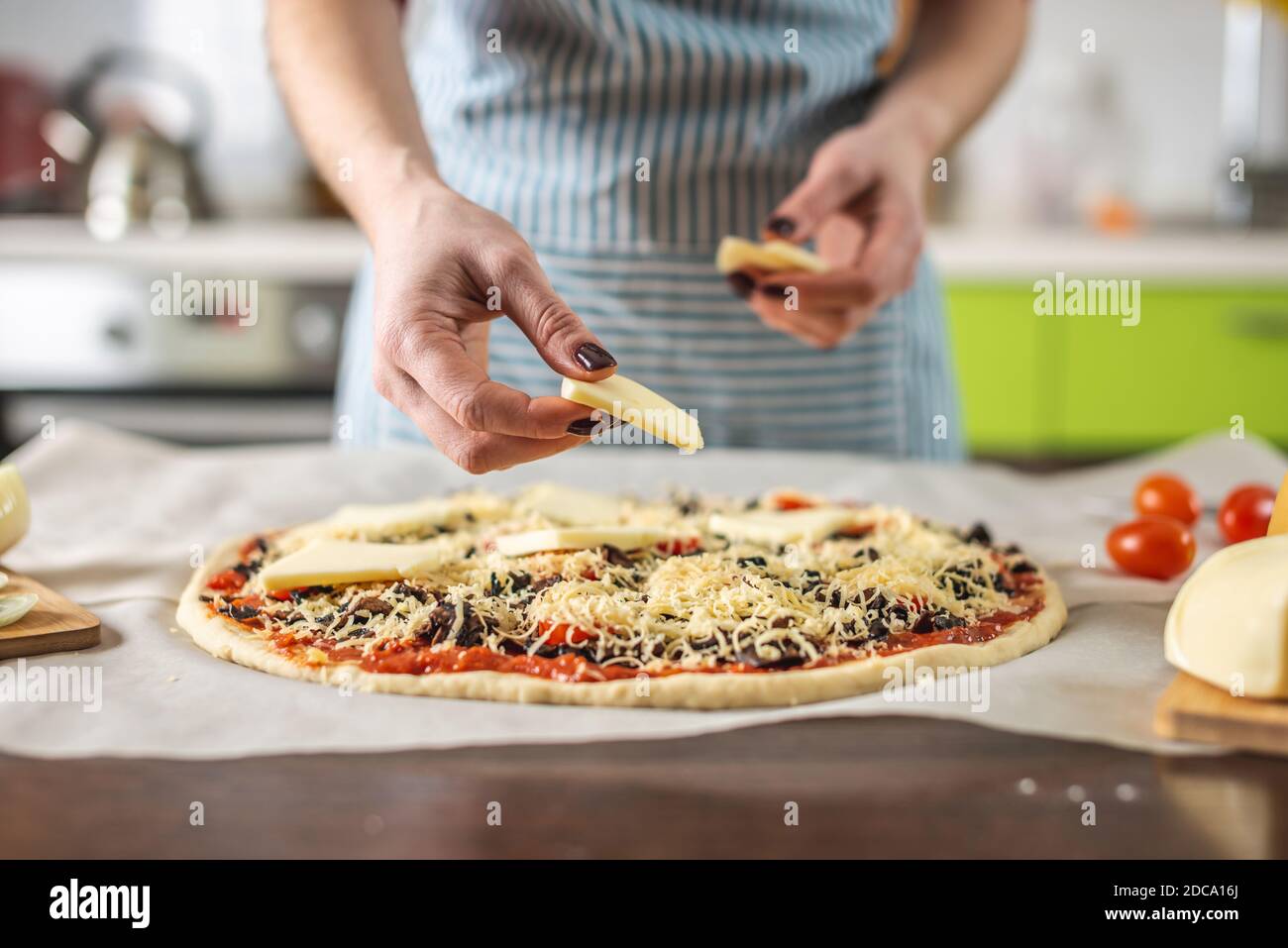 A female chef in an apron is putting mozzarella cheese on a raw pizza ...