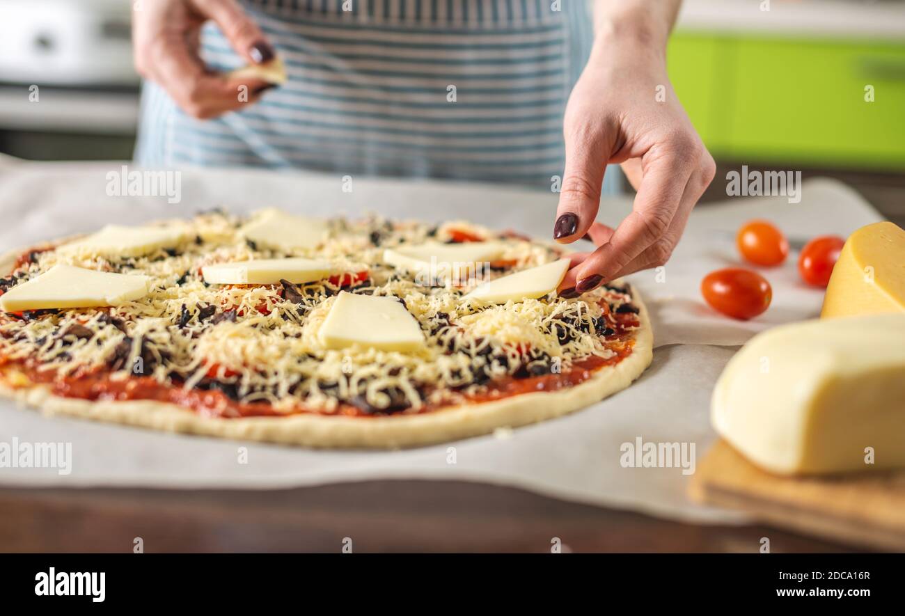 A female chef in an apron is putting mozzarella cheese on a raw pizza ...