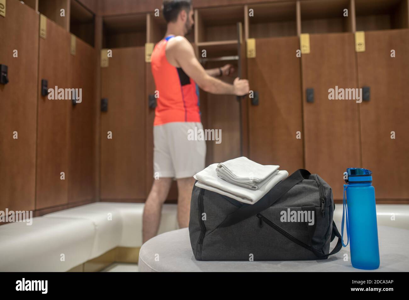 Sporty man in bright tshirt standing near the locker in a changing room ...