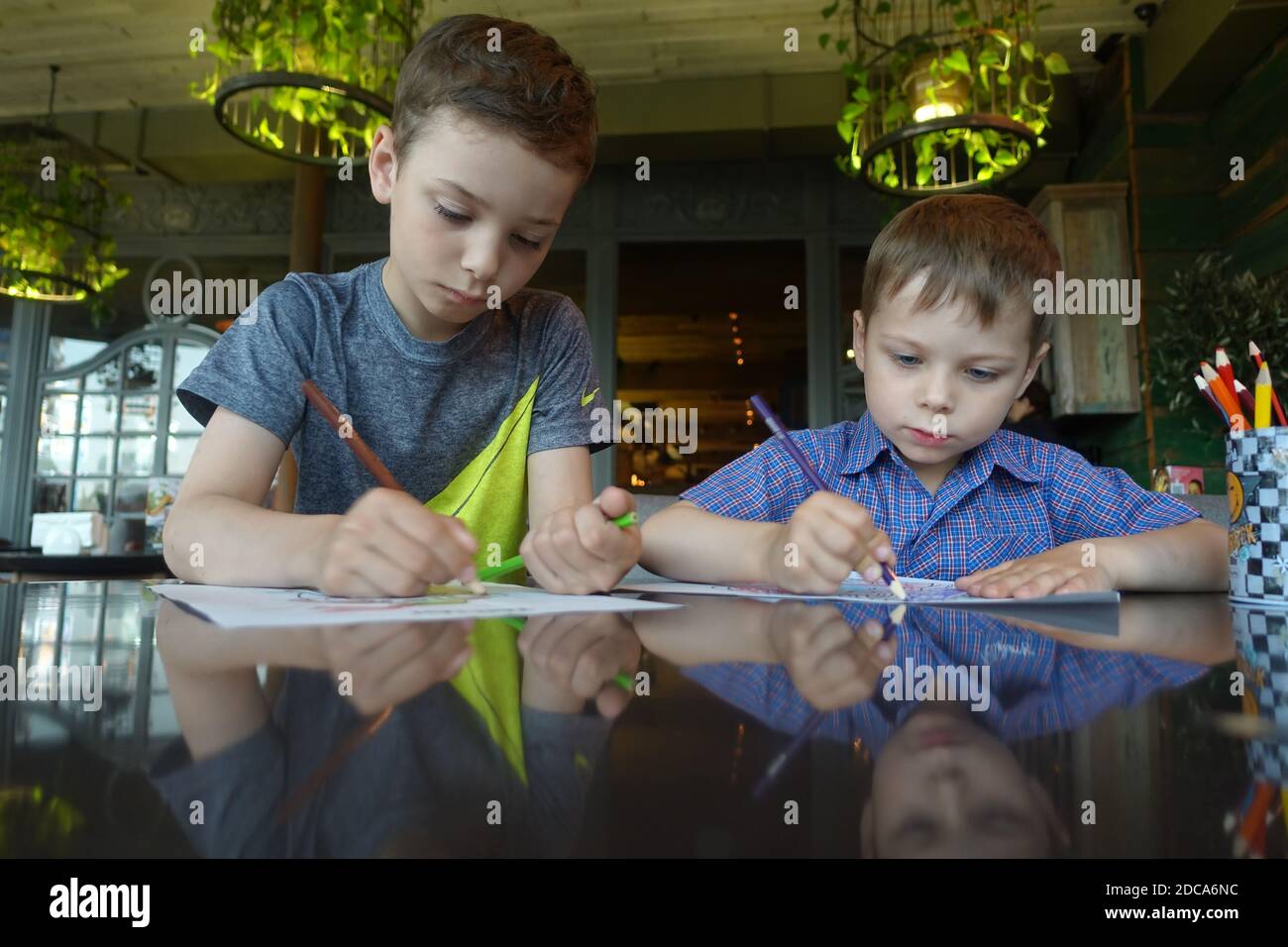 Two brothers drawing with pencil in a cafe Stock Photo - Alamy
