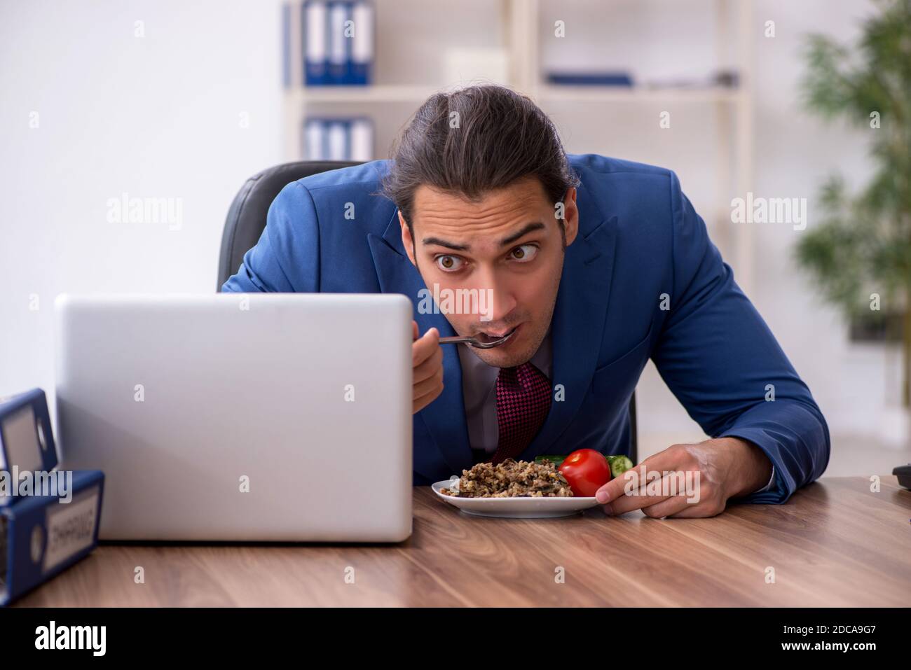 Hungry employee eating buckwheat during break Stock Photo - Alamy